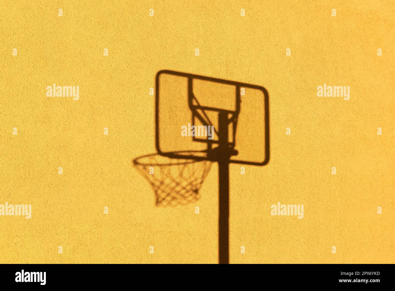 The shadow of a basketball hoop is silhouetted against the yellow wall ...