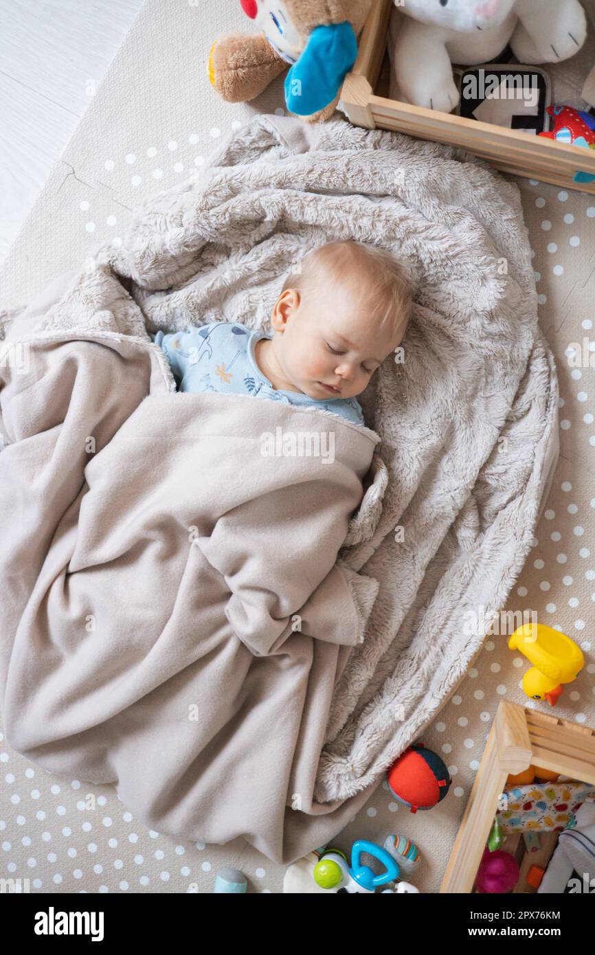 Cute infant baby boy sleeping on playing mat covered with warm cosy ...