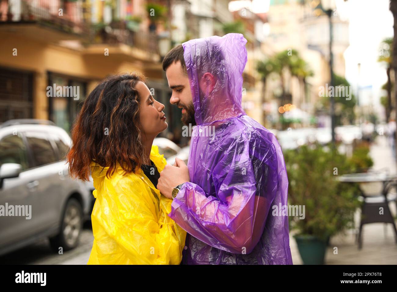 Young Couple In Raincoats Enjoying Time Together On City Street Stock