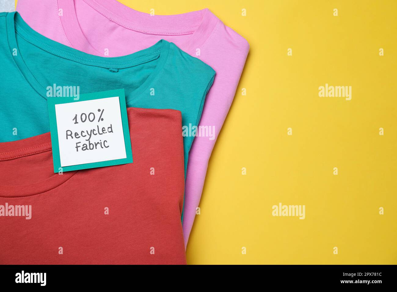Different clothes with recycling label on yellow background, top view ...