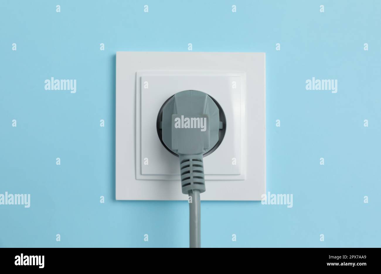 Power socket with inserted plug on light blue wall, closeup. Electrical ...
