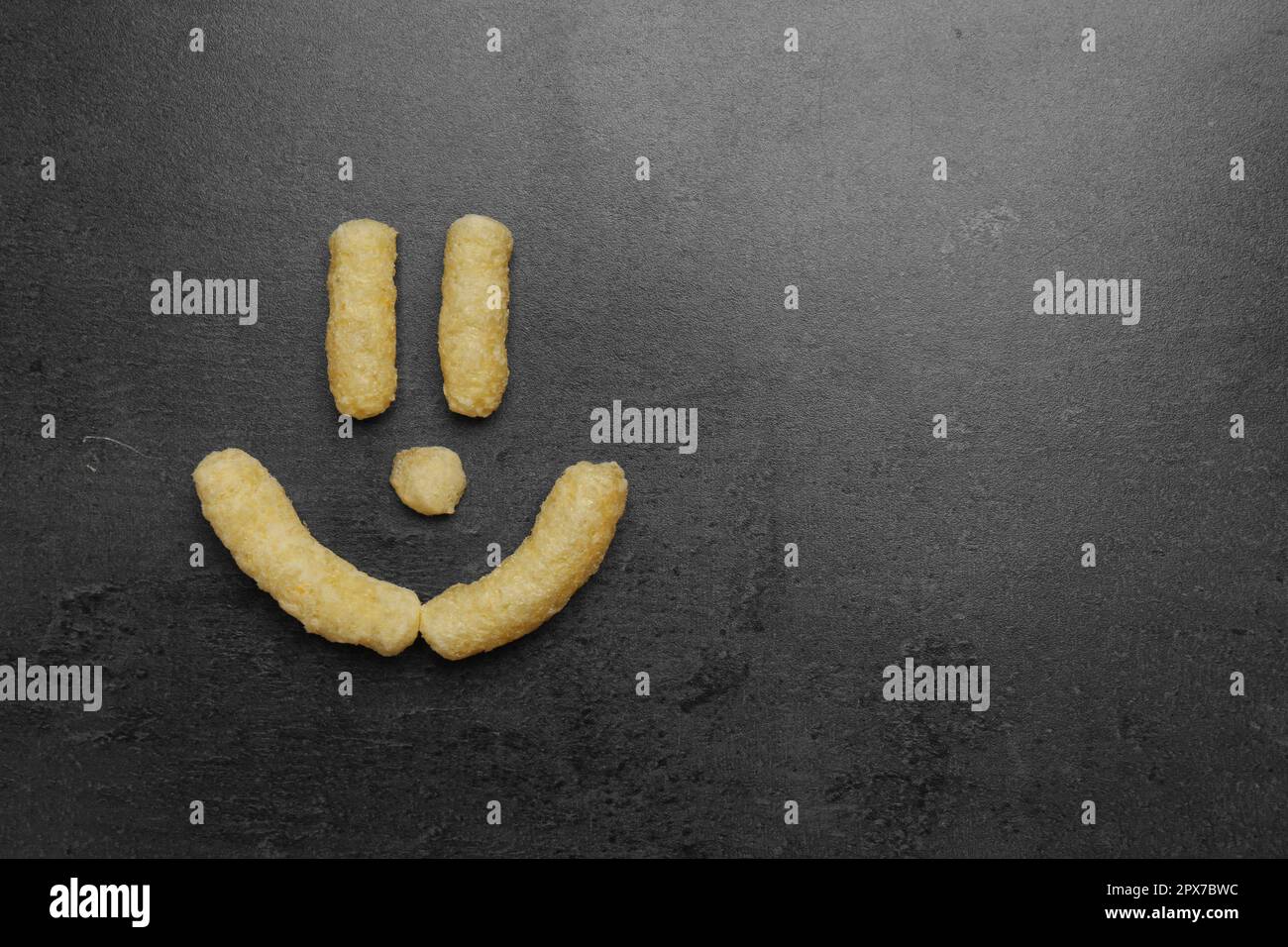 Funny face made of corn sticks on dark grey table, flat lay. Space for ...