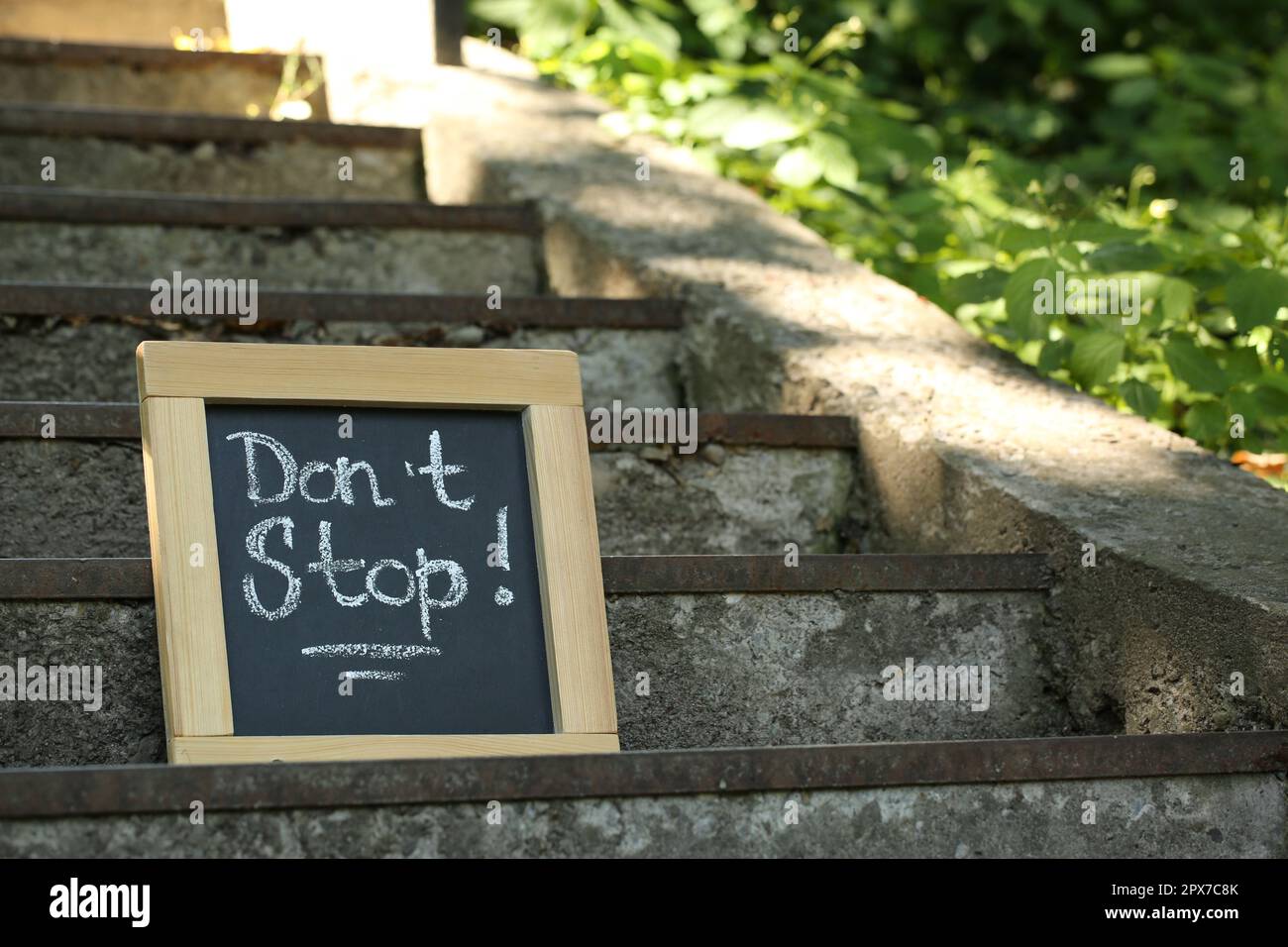 Chalkboard with phrase Don't Stop on stone stairs outdoors, space for ...