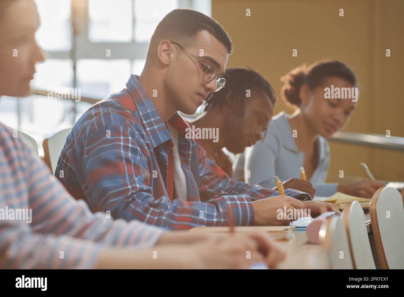 Group of students sitting in a row at desk and studying together at ...