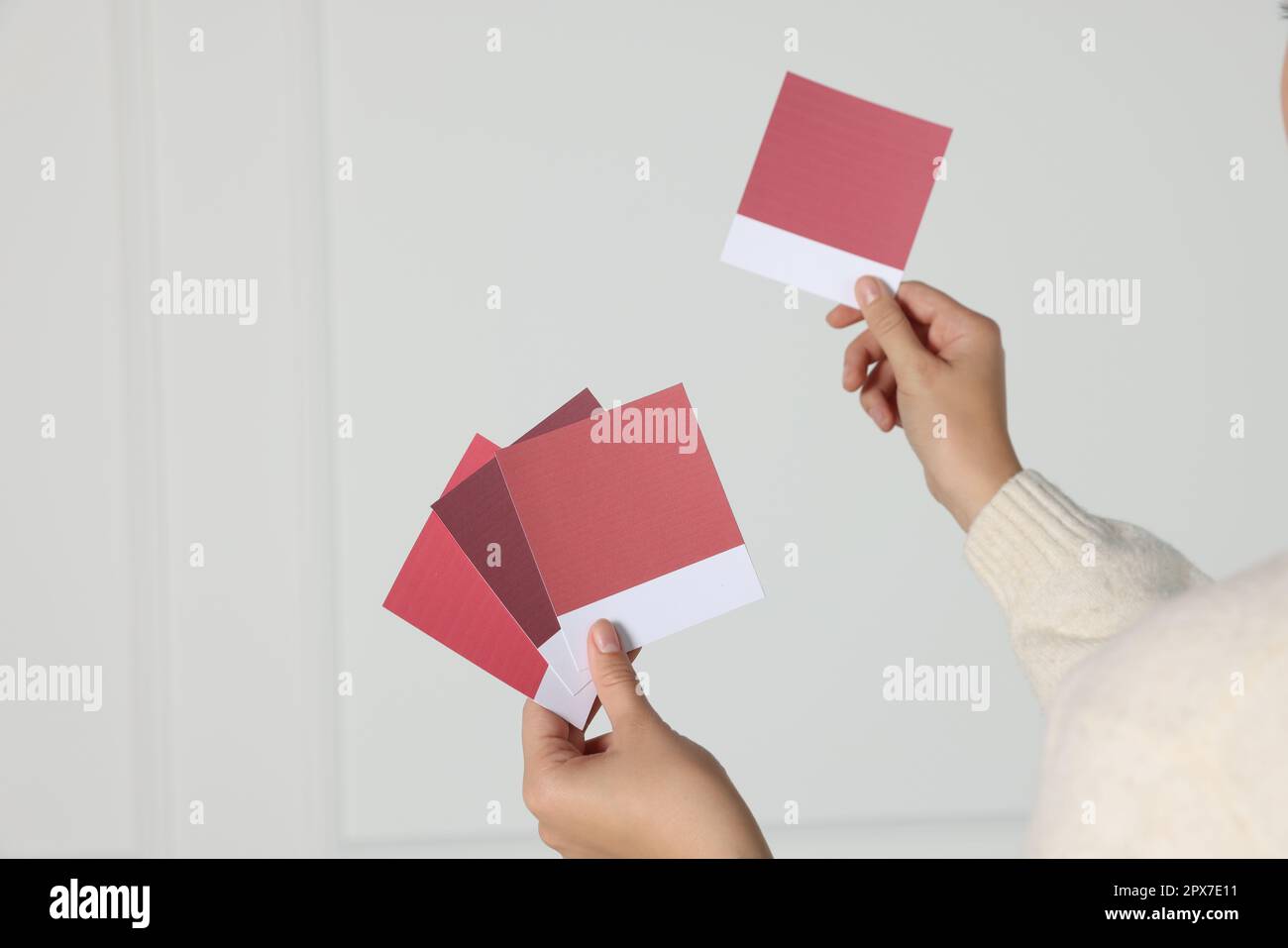 Woman with color sample cards choosing paint shade for wall indoors ...