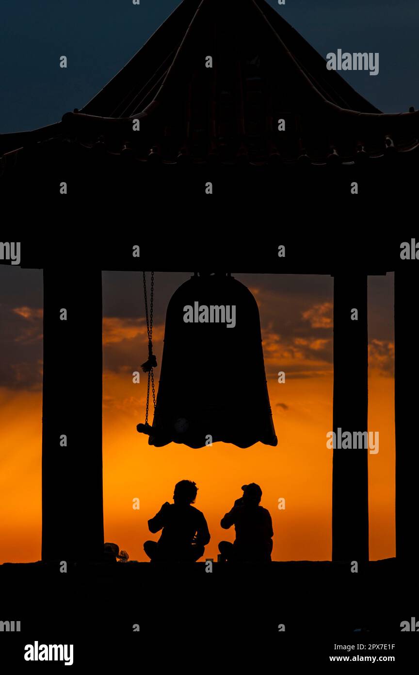Silhouettes of two people meditating under a bell of a Buddhist temple ...