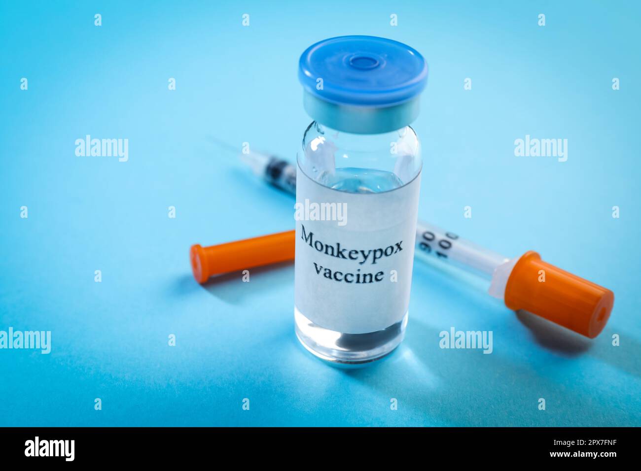 Monkeypox vaccine in glass vial and syringe on light blue background ...