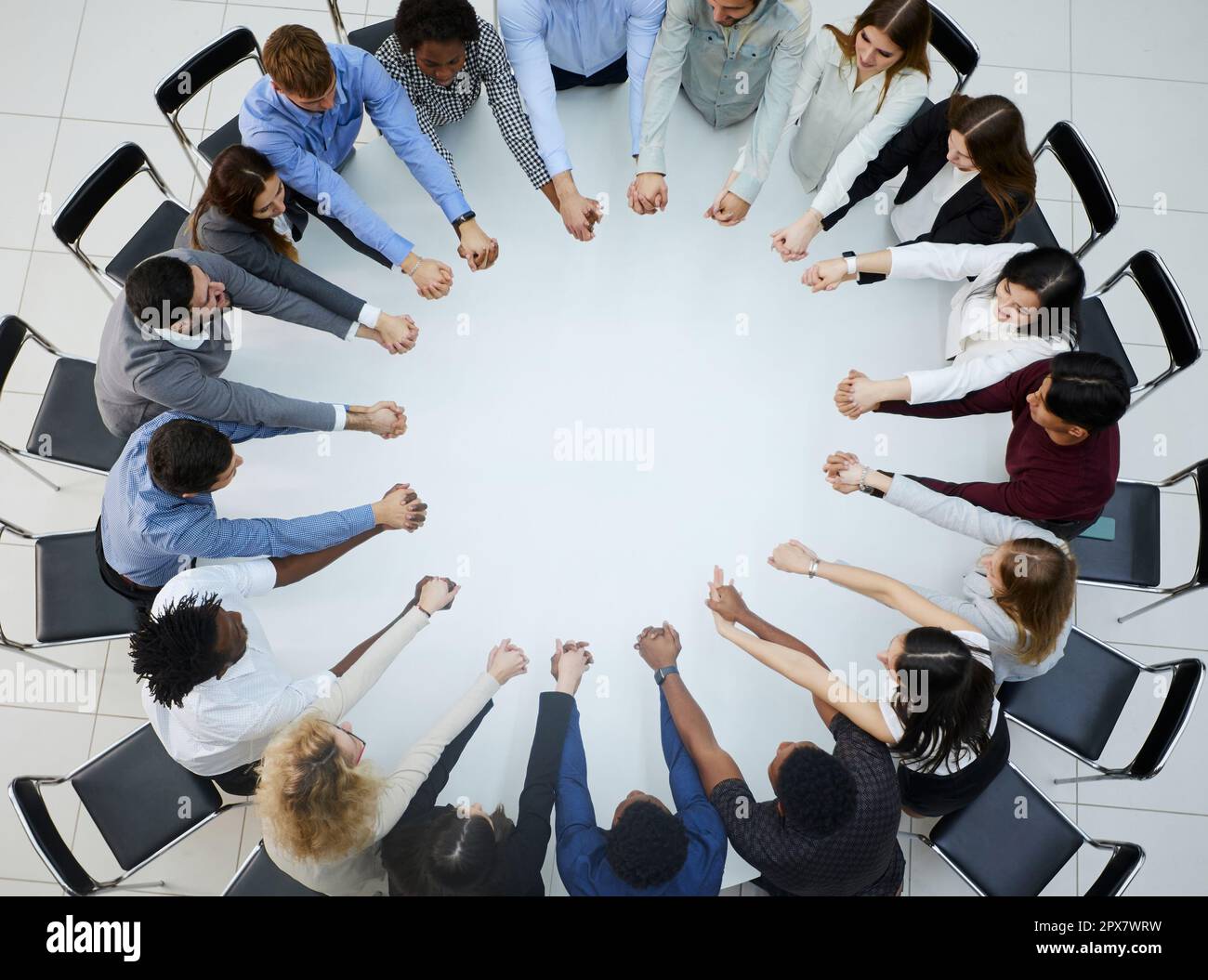 a large group of people sitting at a round table with their arms ...