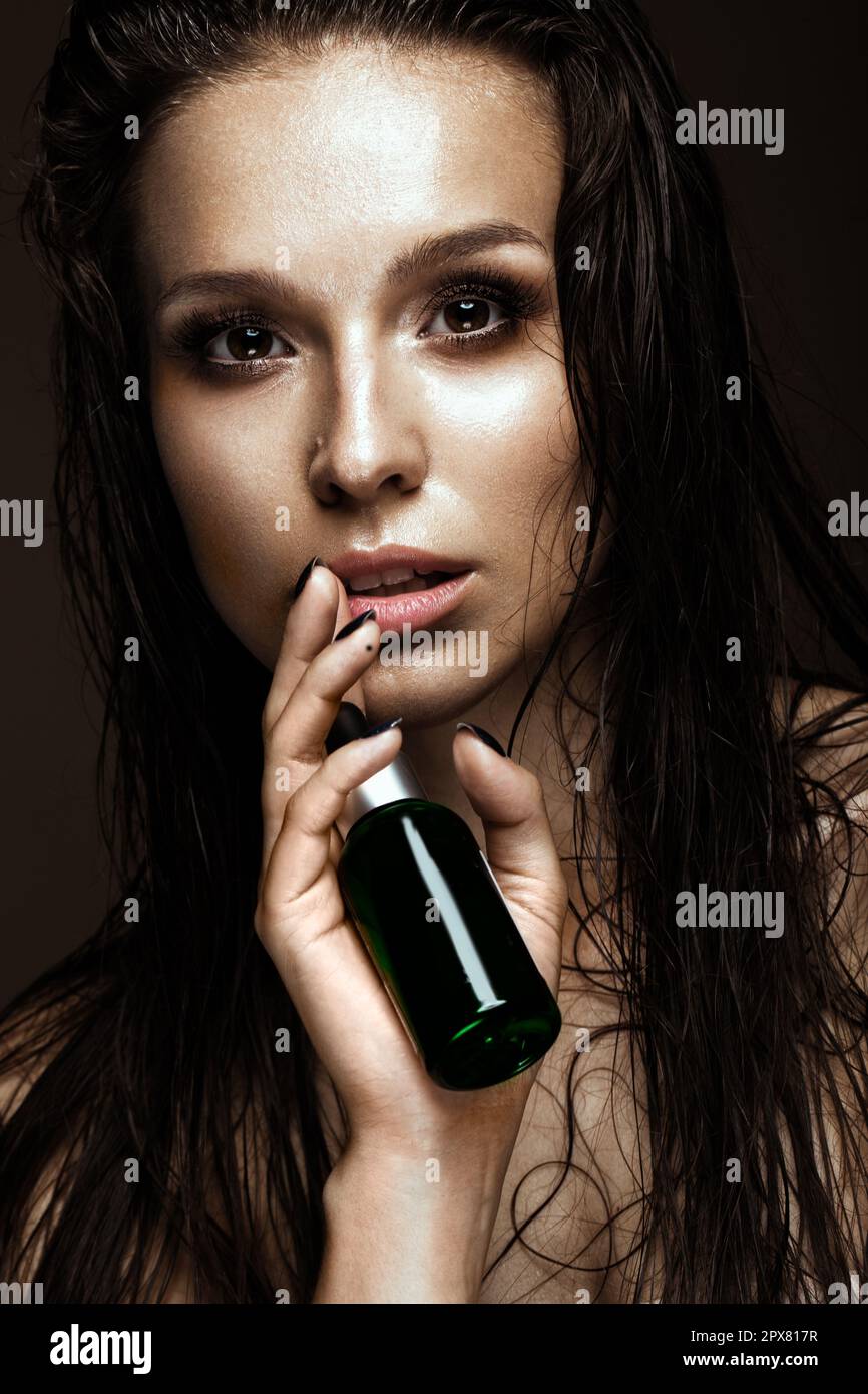 Beautiful girl with a bright make-up and wet hair and skin with bottle ...