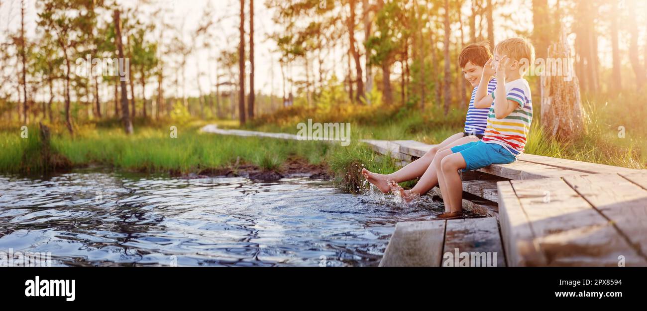 Two boys sitting on the pier of the swamp lake and making splashes by ...