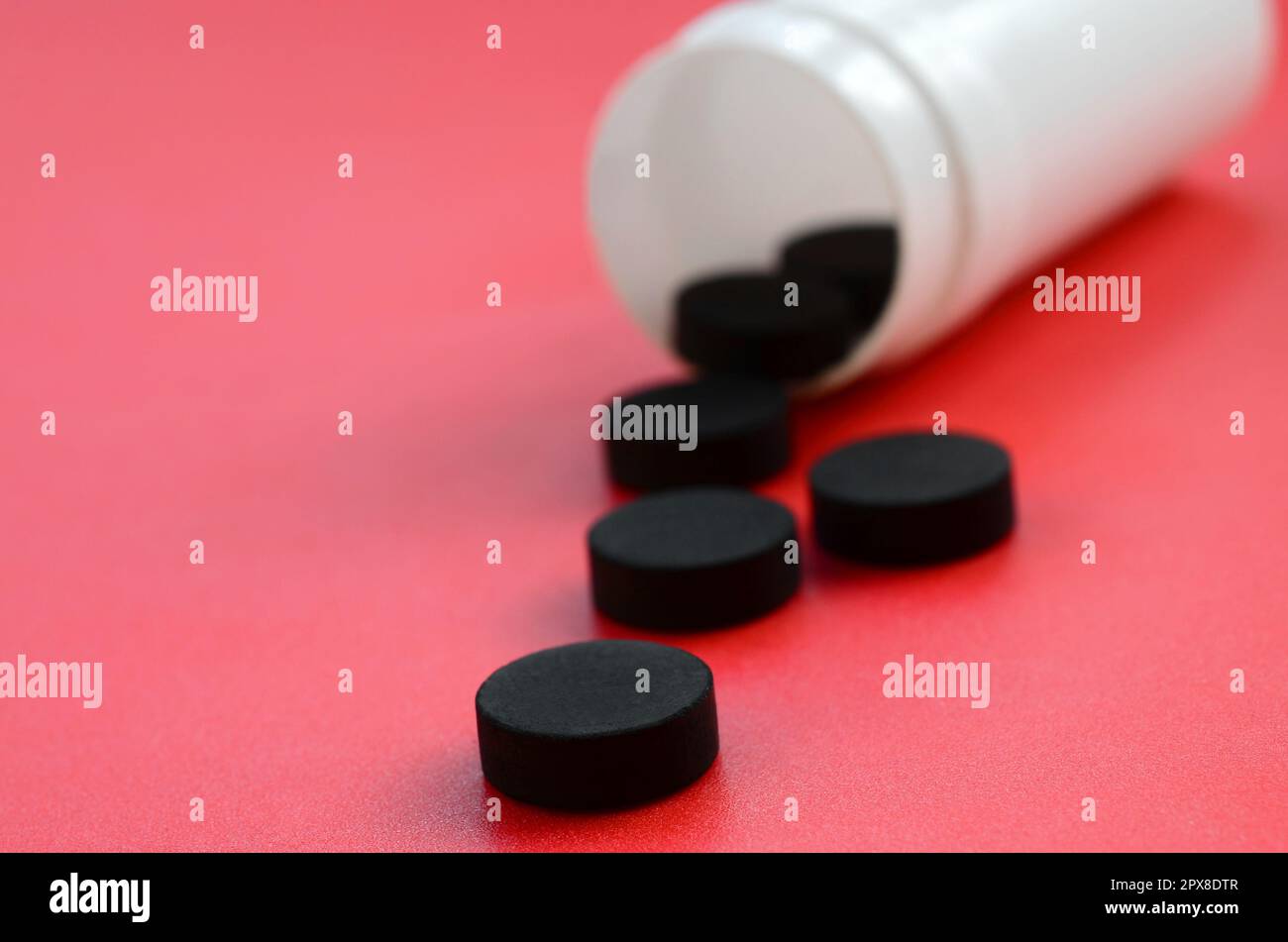 Several black tablets fall out of the plastic jar on the red surface ...
