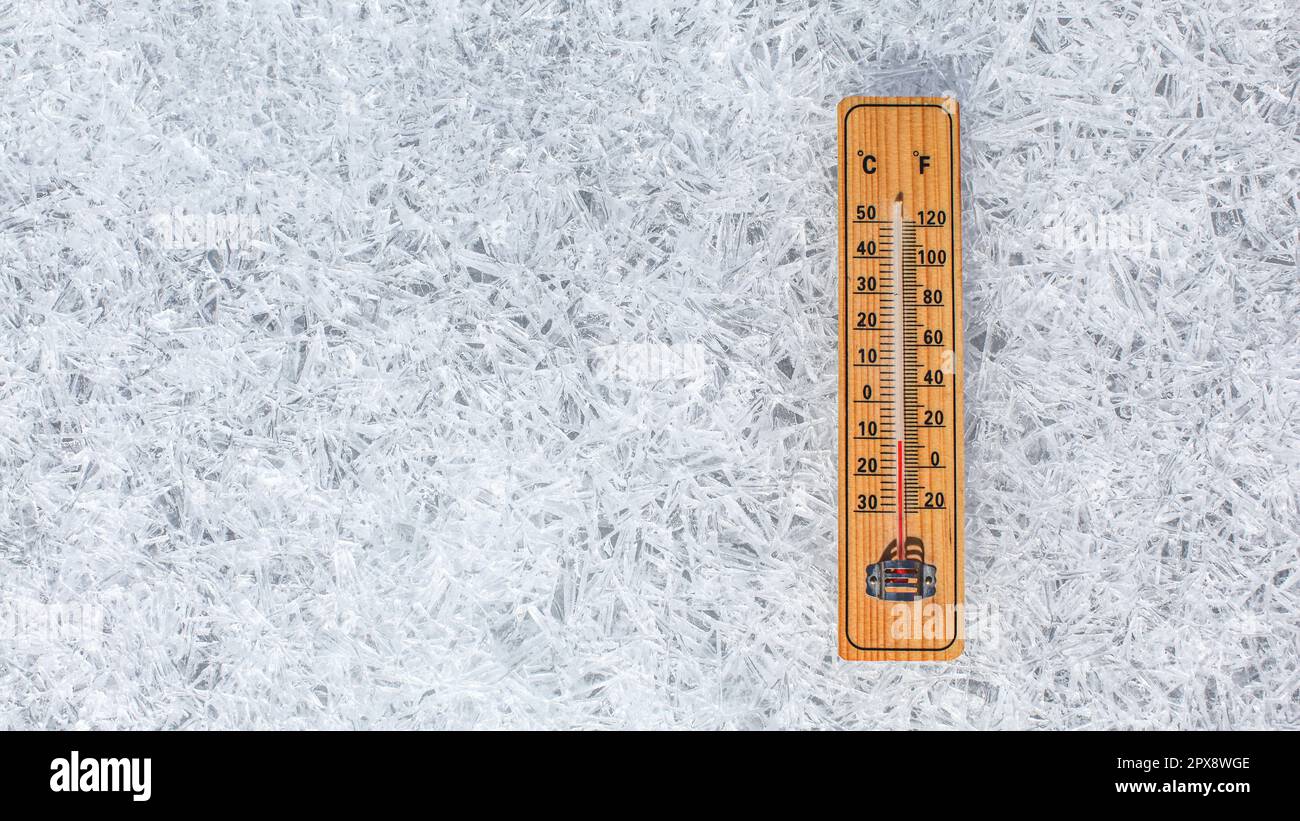 Wooden thermometer showing low temperature laying on flat ice ground ...