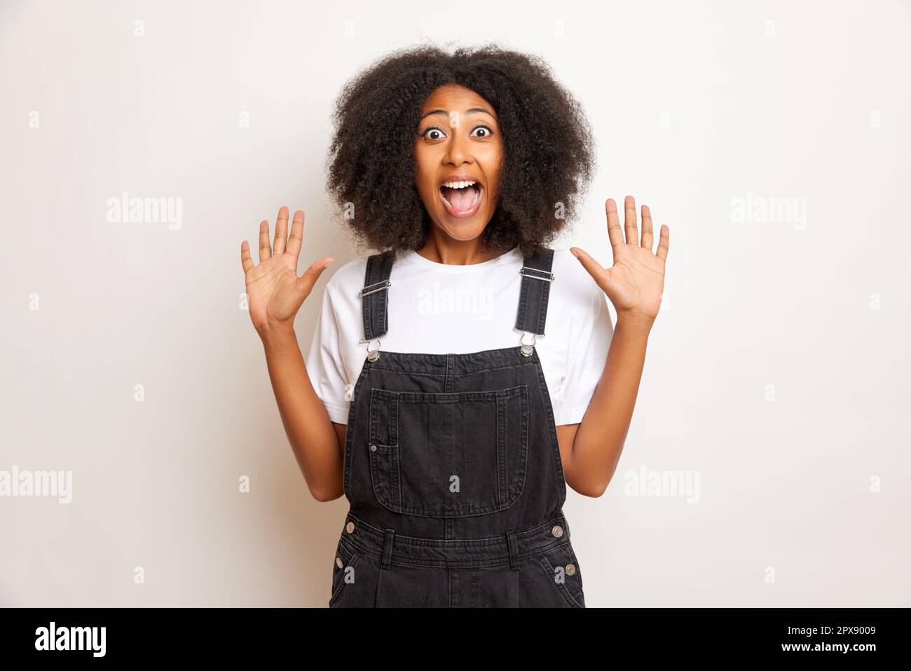 Emotional dark skinned curly haired female model keeps palms raised ...