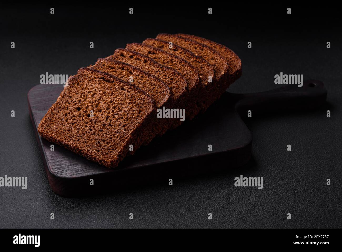 Delicious fresh brown bread with grains and seeds sliced on a wooden cutting board on a dark ...