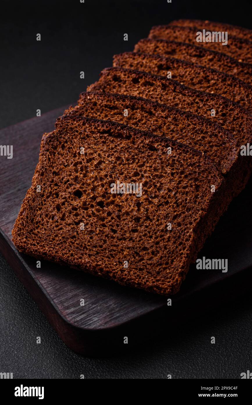 Delicious fresh brown bread with grains and seeds sliced on a wooden cutting board on a dark ...