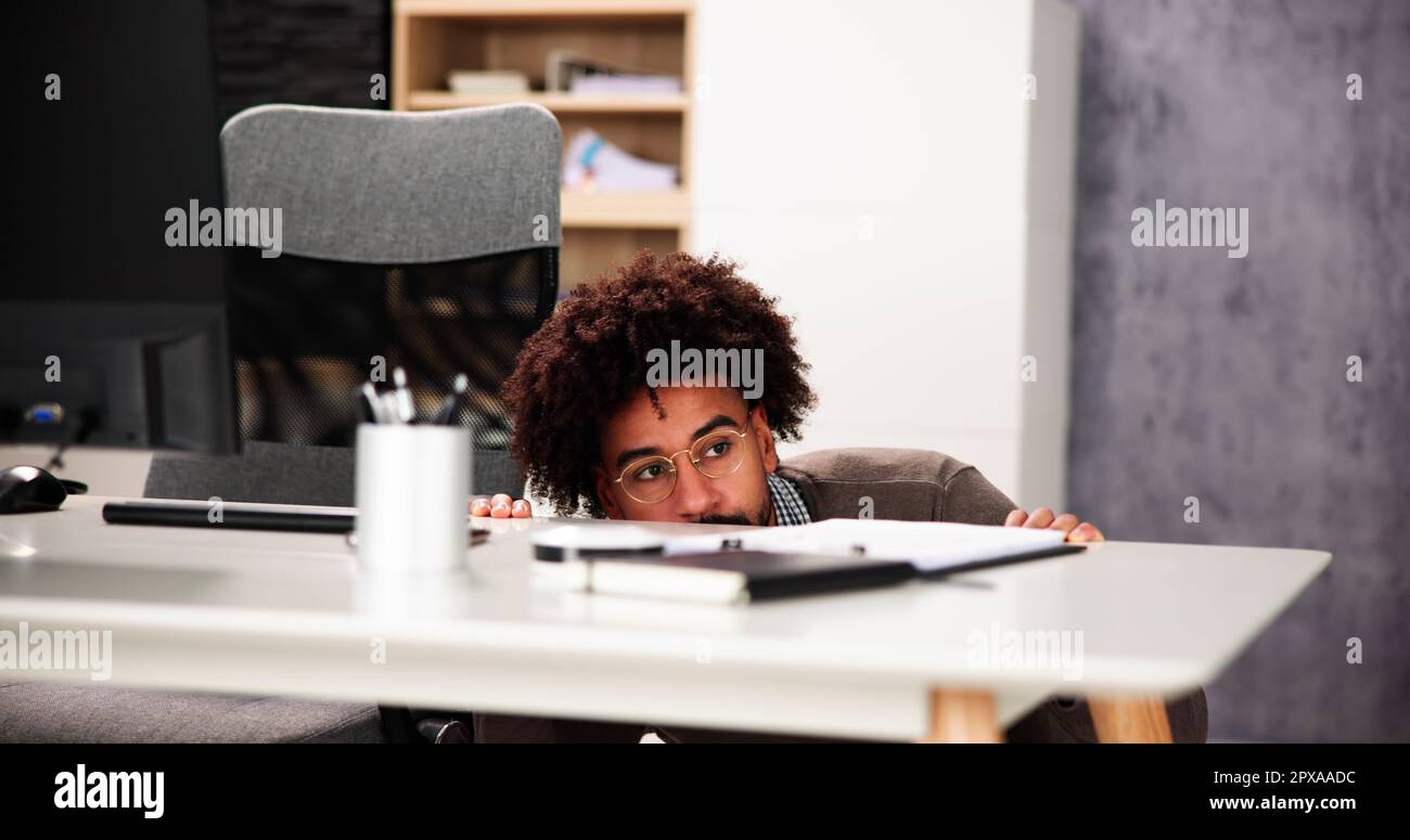 Scared Man Hiding Behind Office Desk In Room Stock Photo - Alamy
