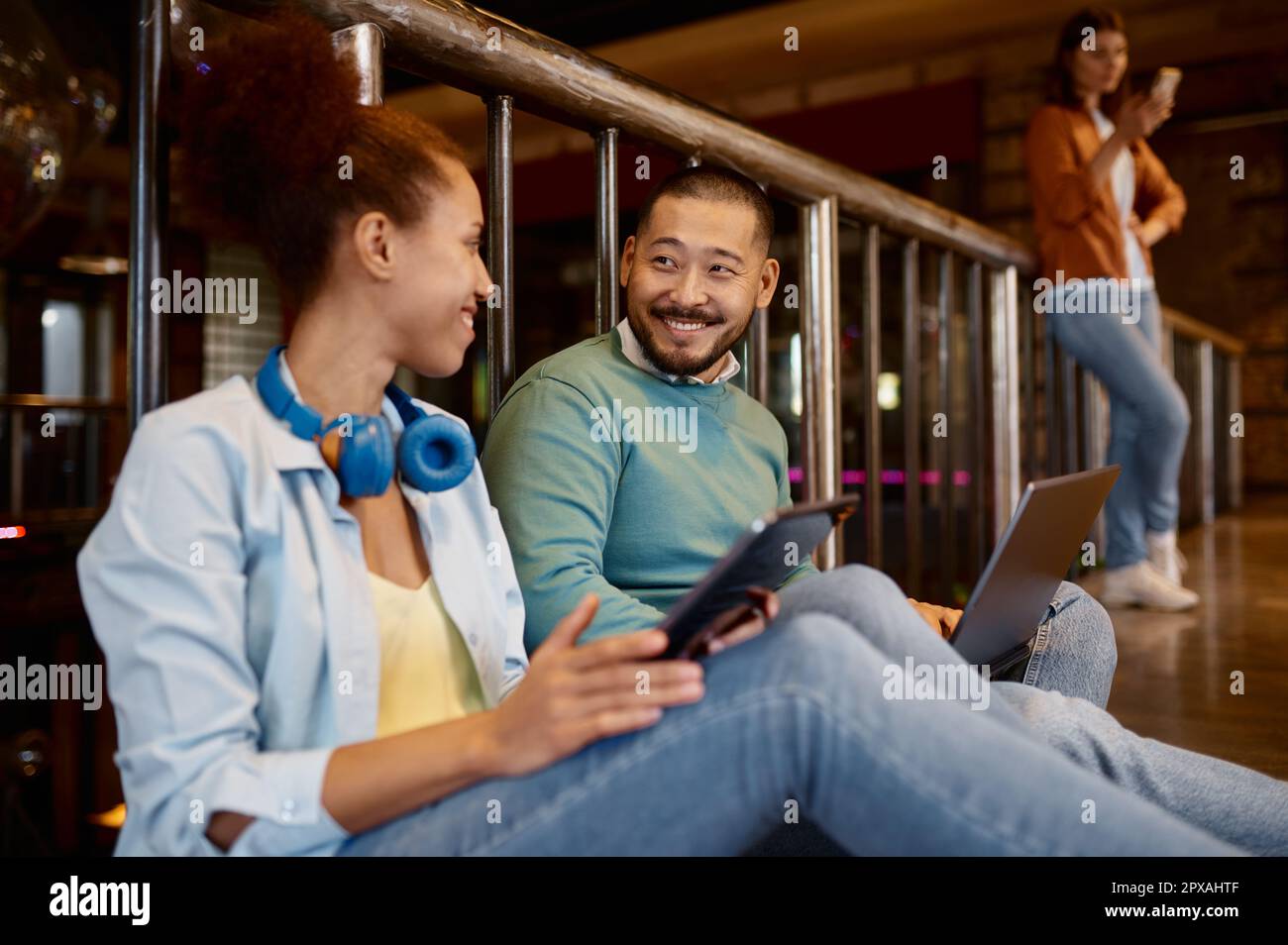 Diverse coworkers sitting on floor talking while using digital tablets ...