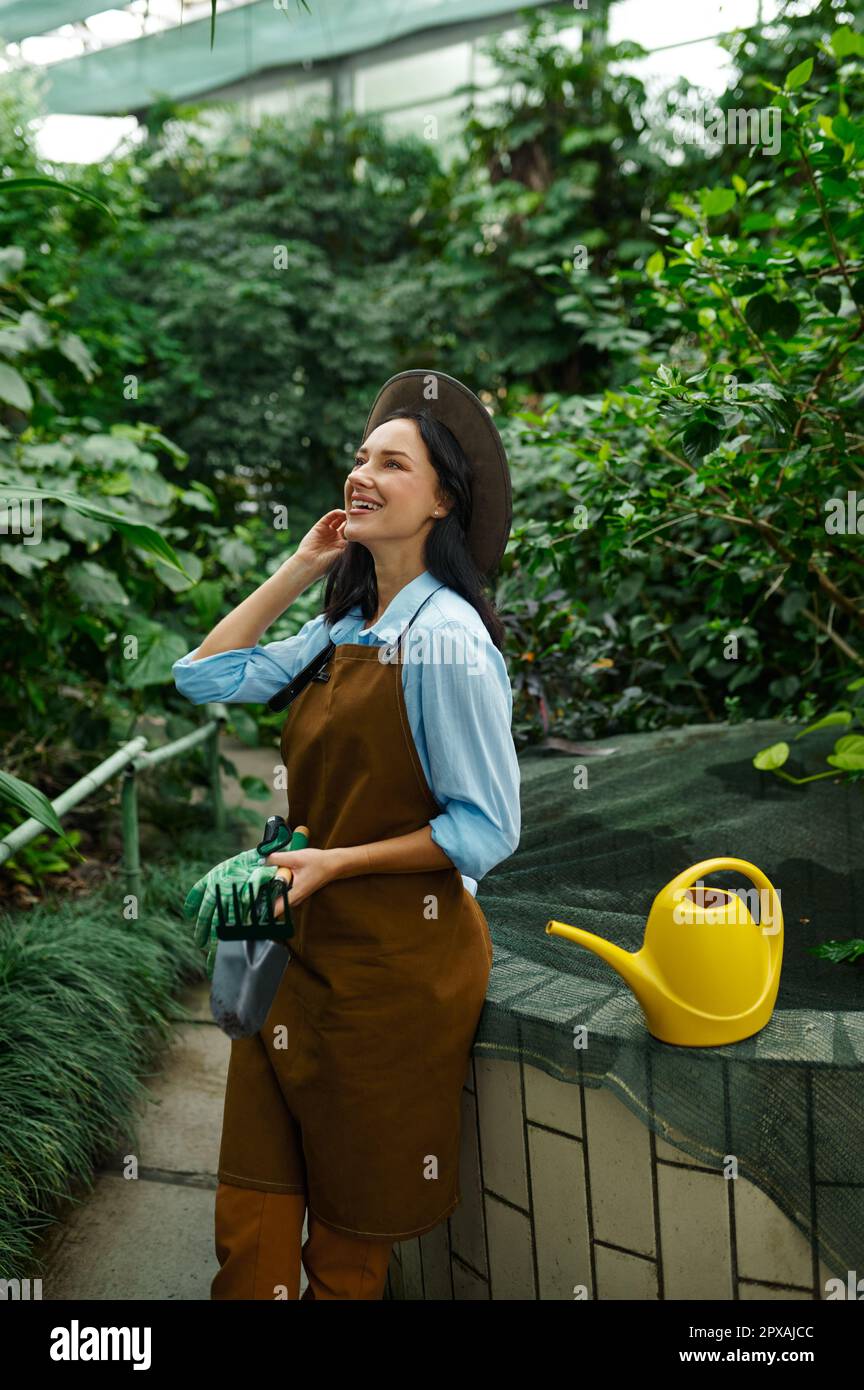 Relaxed tired young woman gardener botanist looking at her beautiful fresh green garden with ...