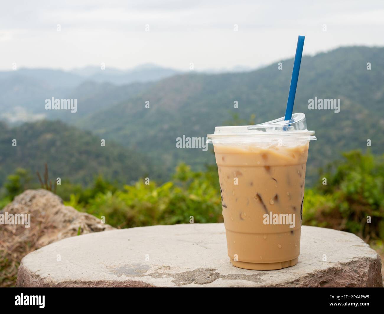 A glass of iced coffee is placed on a rock against a background of ...