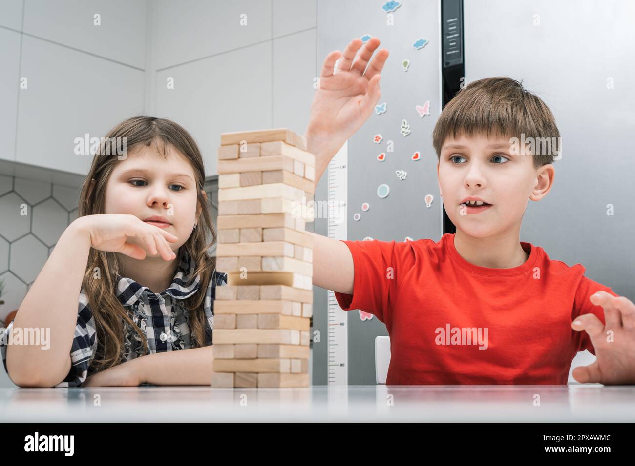 Two children friends playing board game Jenga on table in kitchen at ...