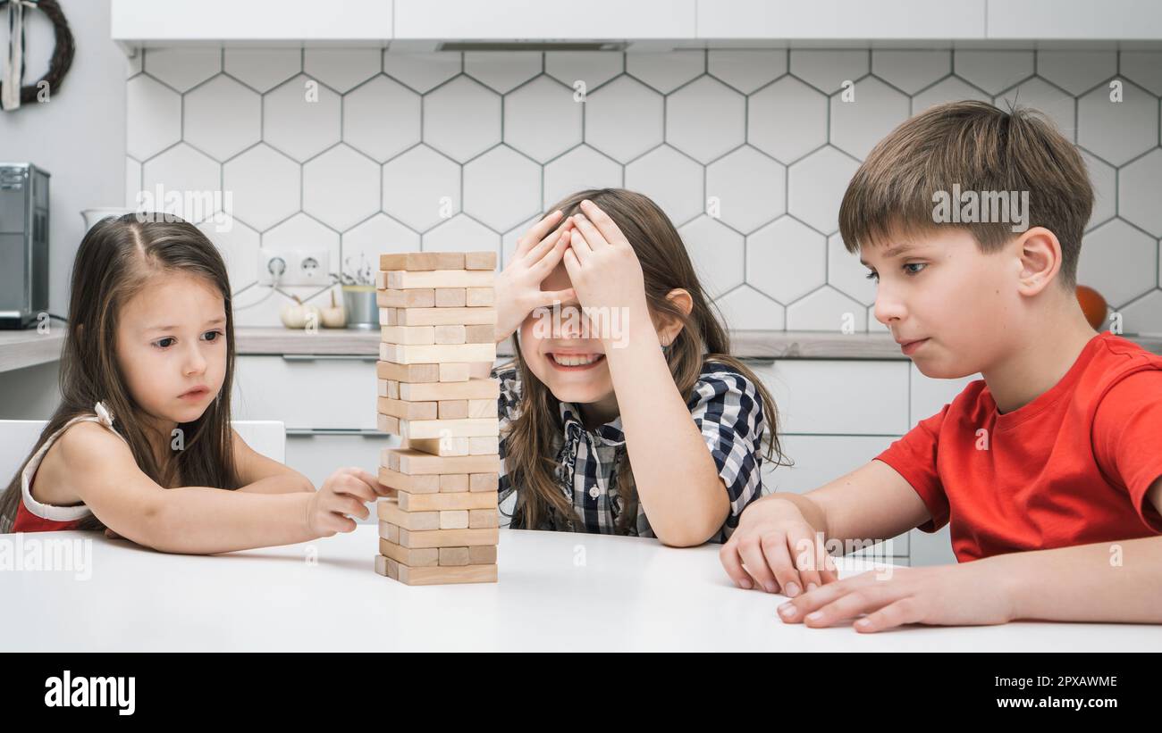 Group of focused children playing board game Jenga on table in kitchen ...