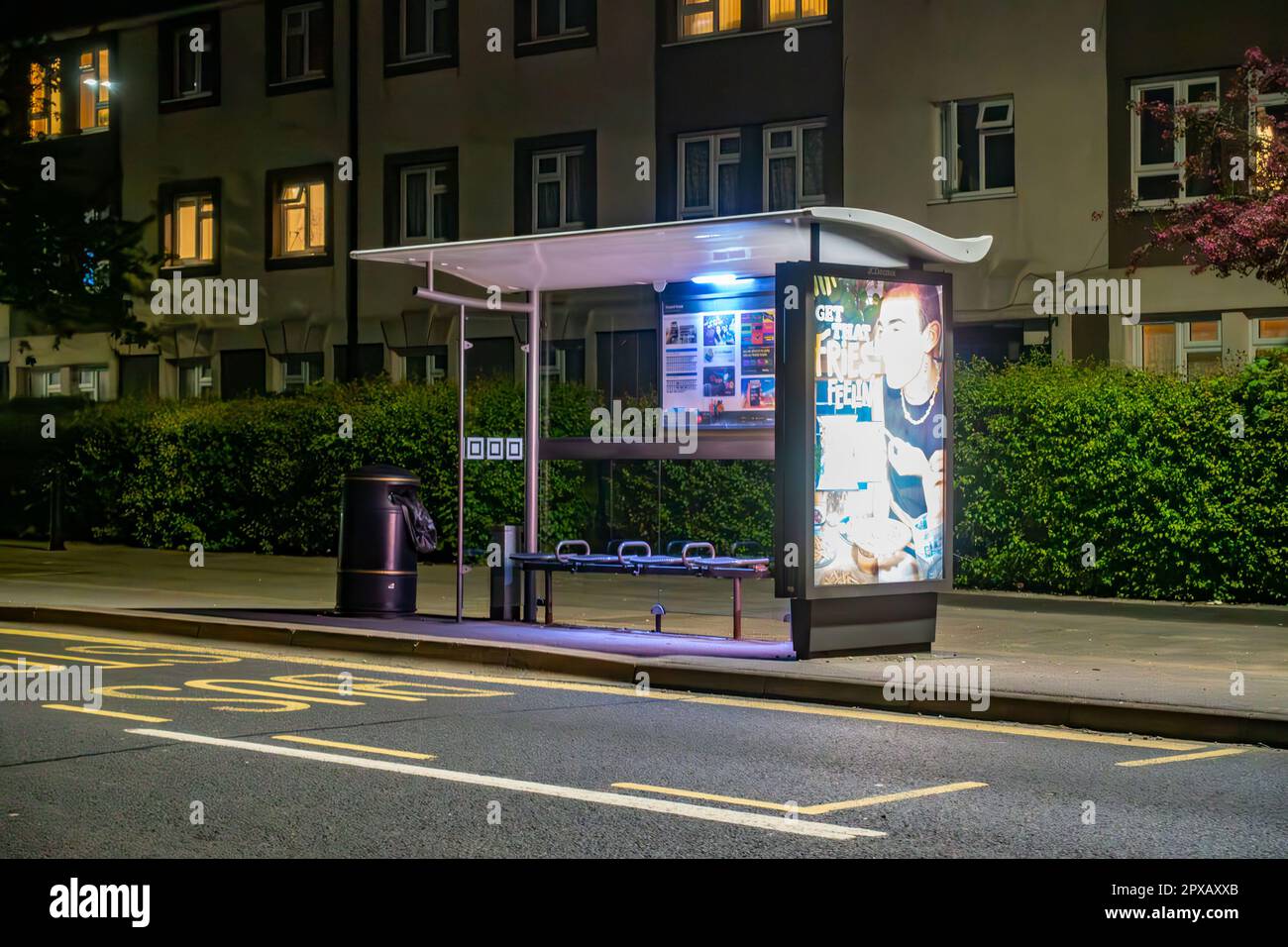 A bus stop with bus shelter lit up at the side of the road at night ...