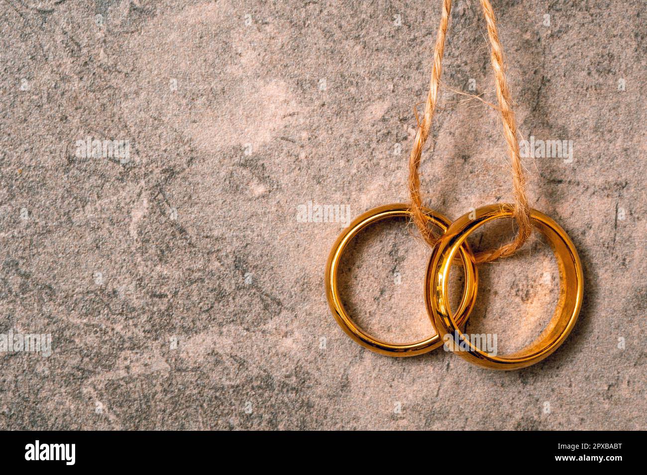 Wedding rings hanging on rope over grey stone background. Love and ...