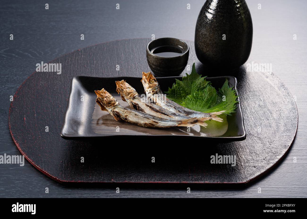 Grilled urume sardines on a black table. A side dish of sake. Japanese ...