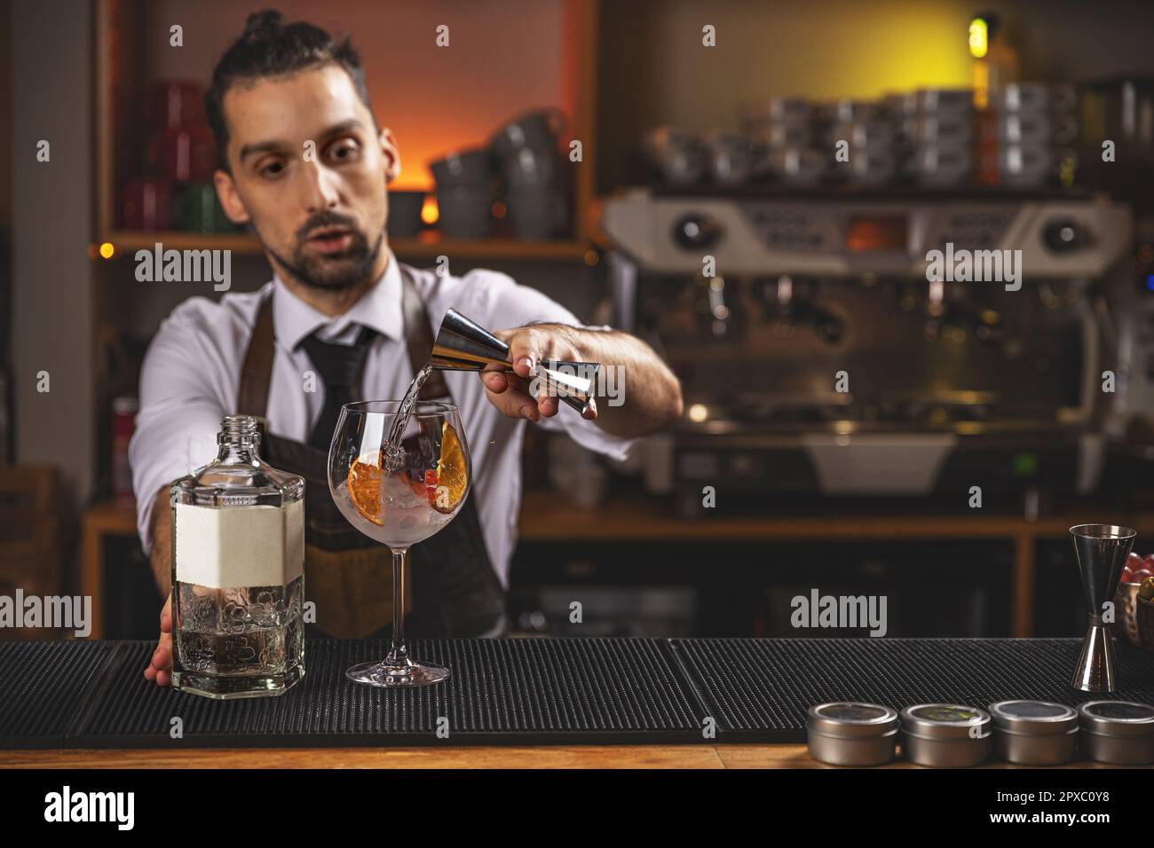 Bartender pouring drink from measuring cup into a cocktail glass filled with ice cubes Stock ...