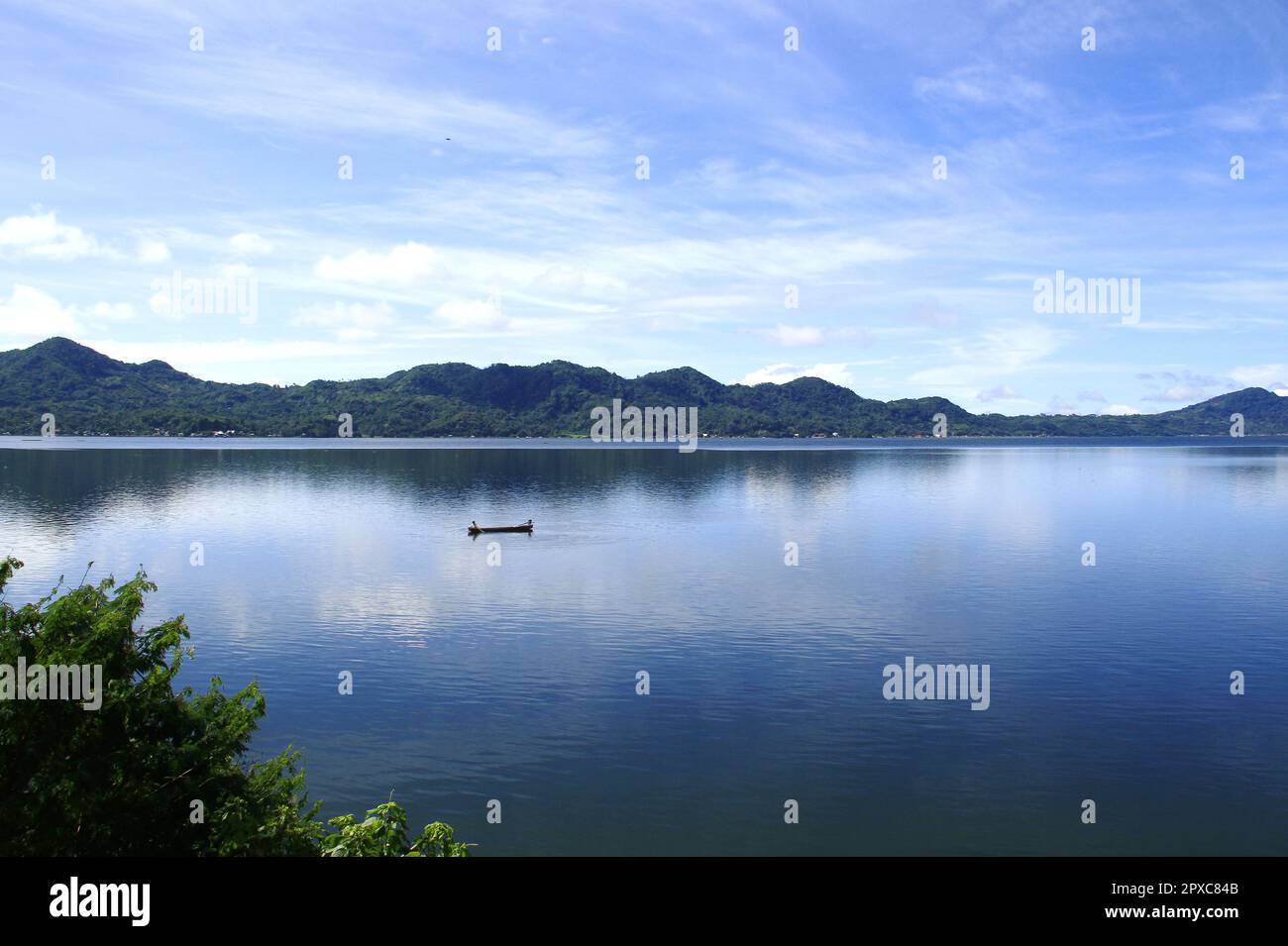 A boat in the middle of a very shady lake, with shades of blue all ...