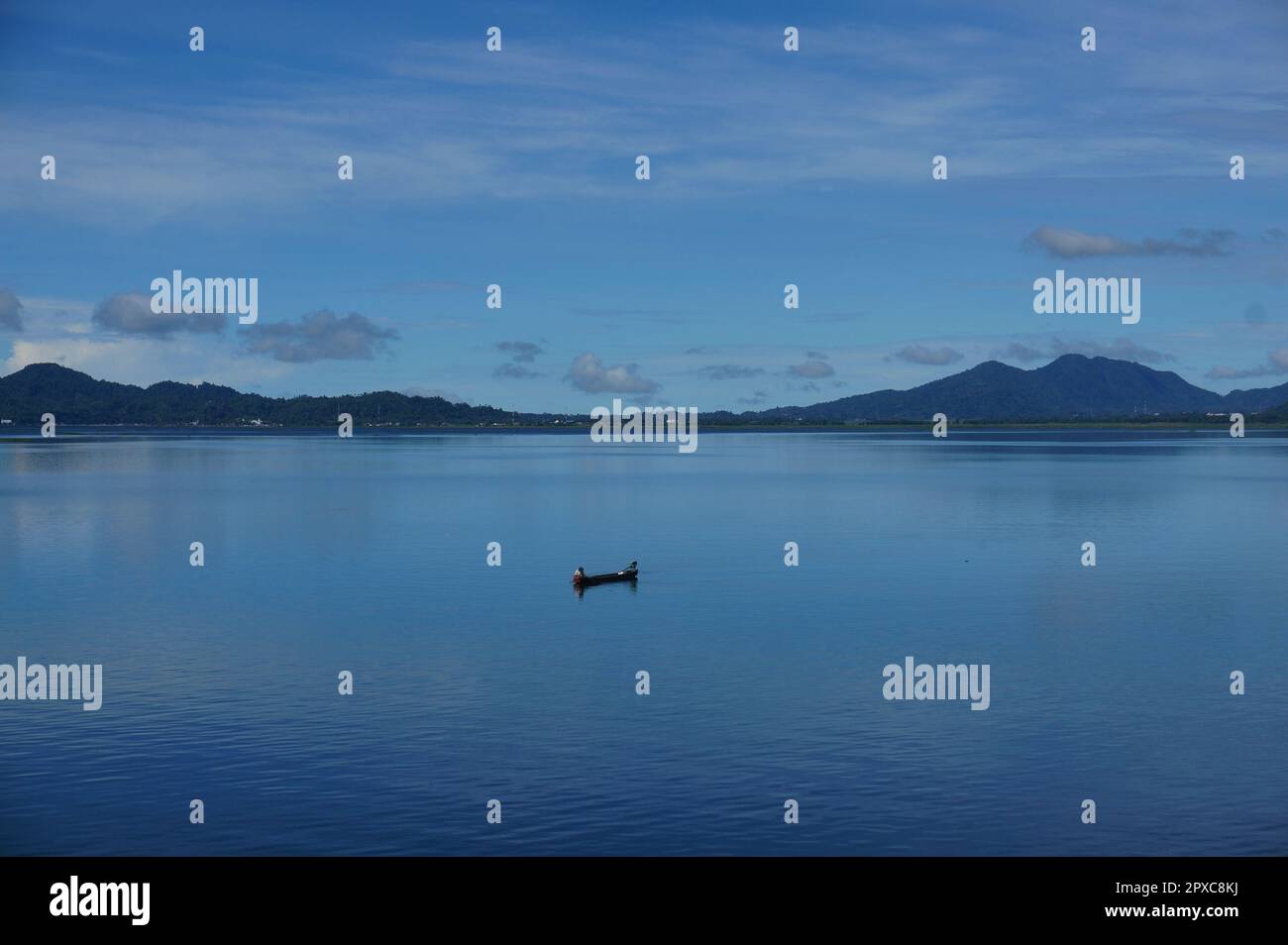 A boat in the middle of a very shady lake, with shades of blue all ...