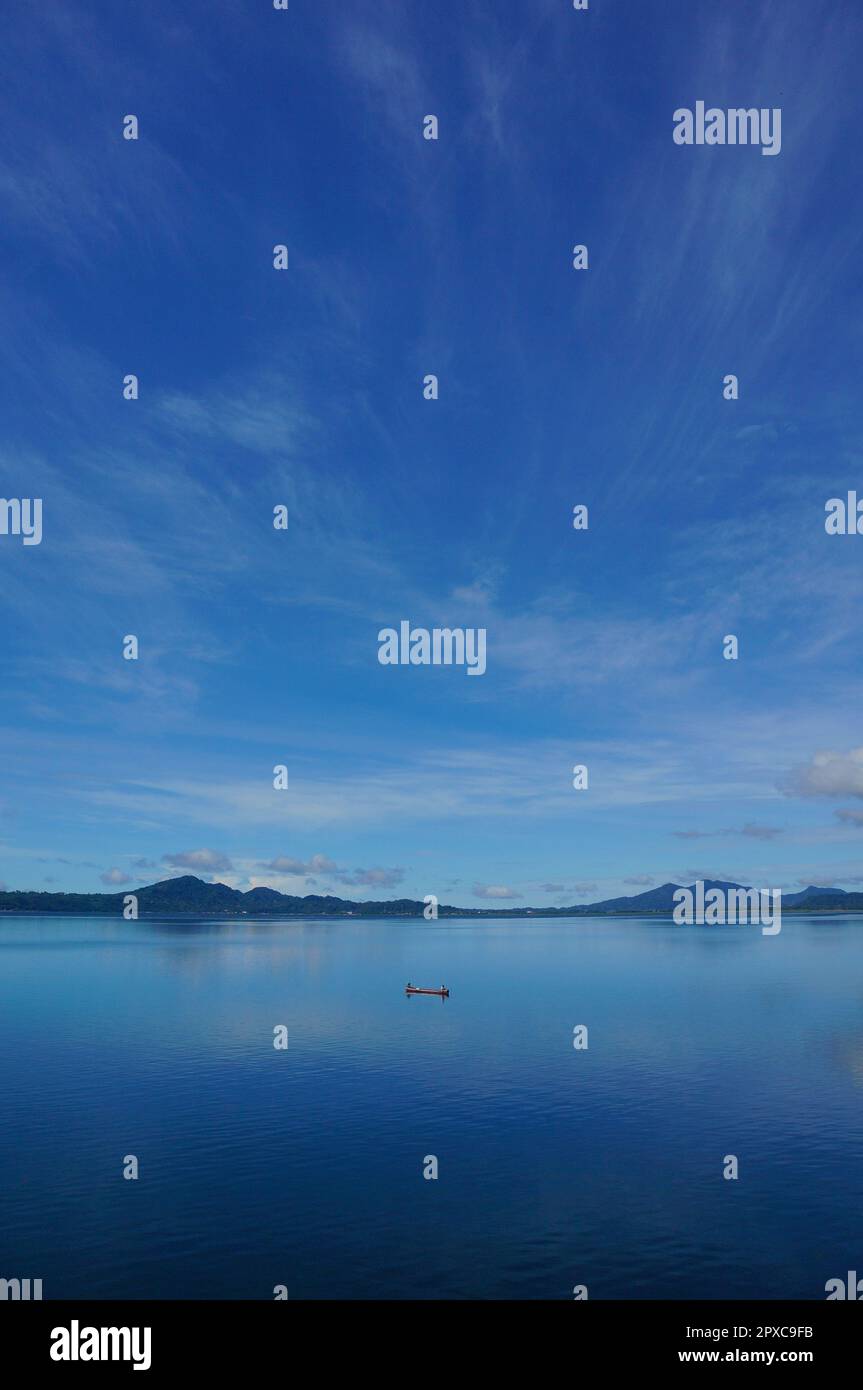 A boat in the middle of a very shady lake, with shades of blue all ...