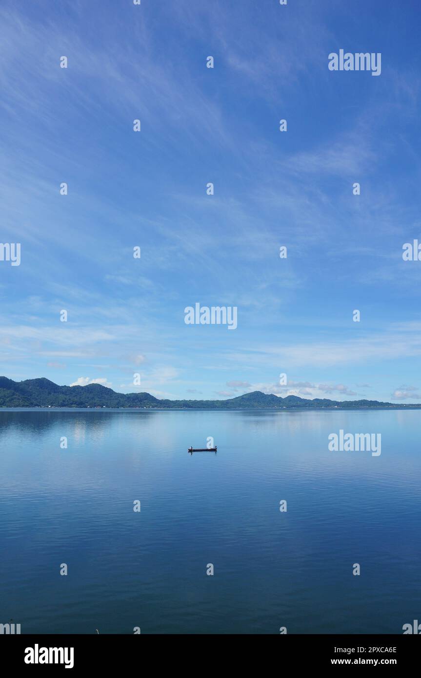 A boat in the middle of a very shady lake, with shades of blue all ...
