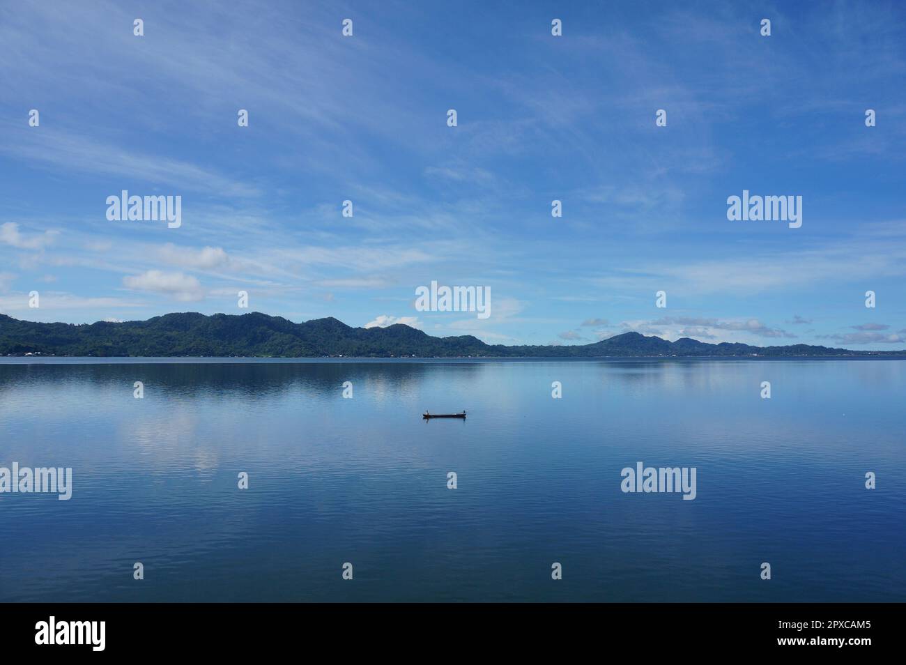 A boat in the middle of a very shady lake, with shades of blue all ...
