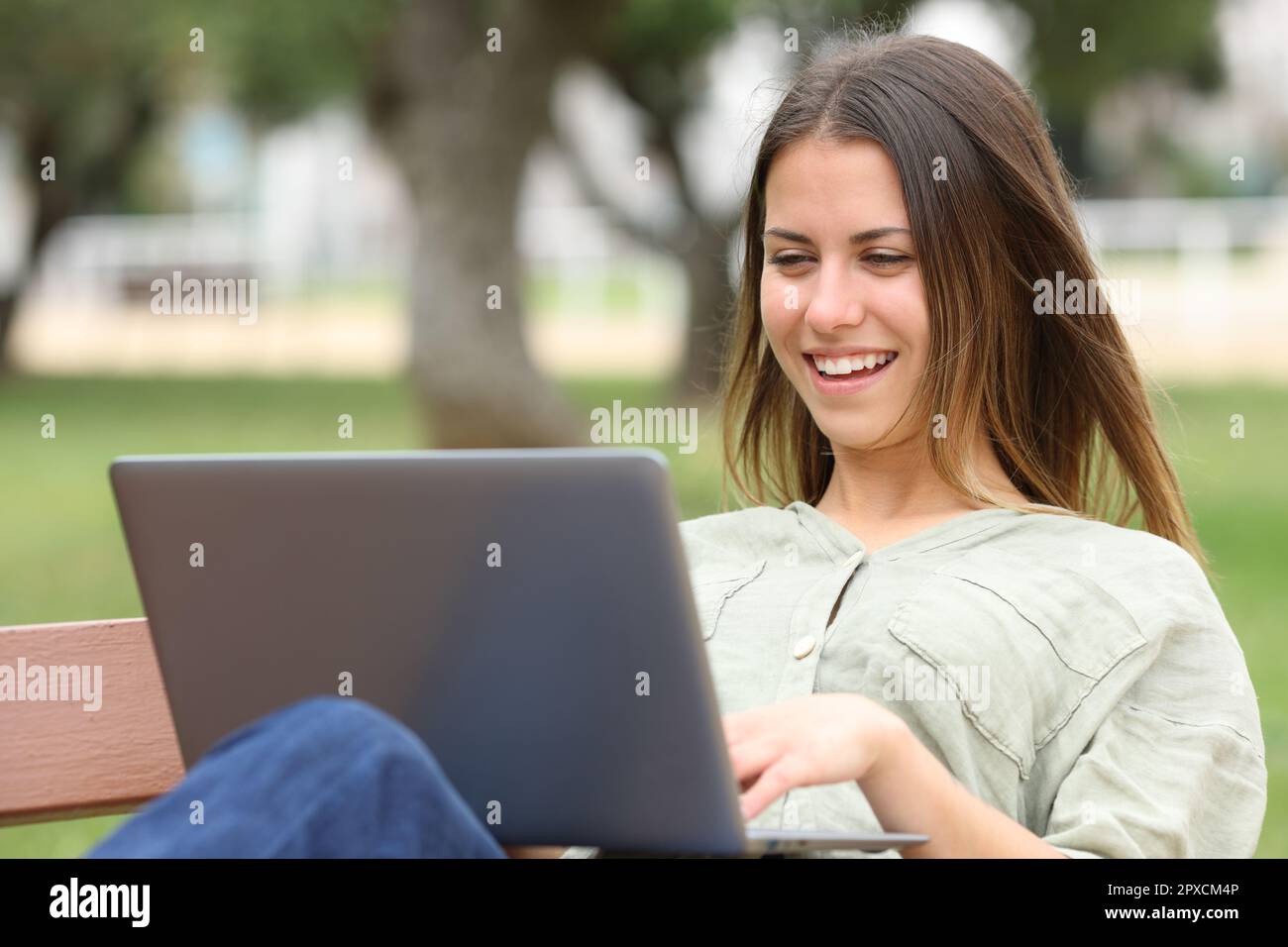 Happy teen using laptop sitting on a bench in a park Stock Photo - Alamy