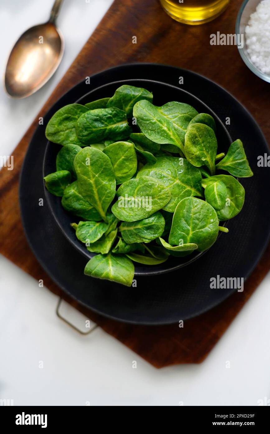 Fresh baby spinach in a black bowl, silver cutlery on an old wooden ...