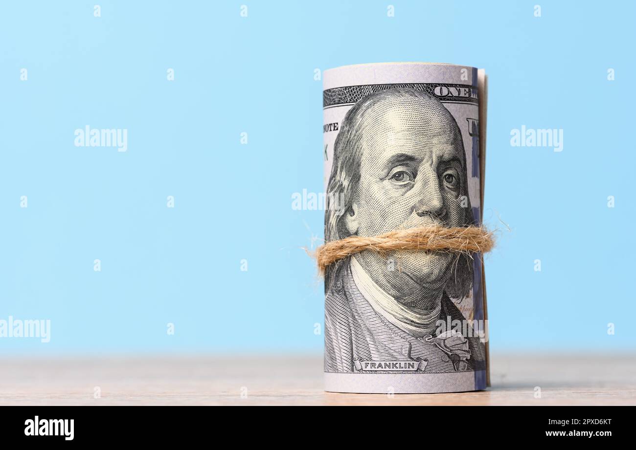 Rope tied roll of one hundred dollar bills on a blue background, copy ...