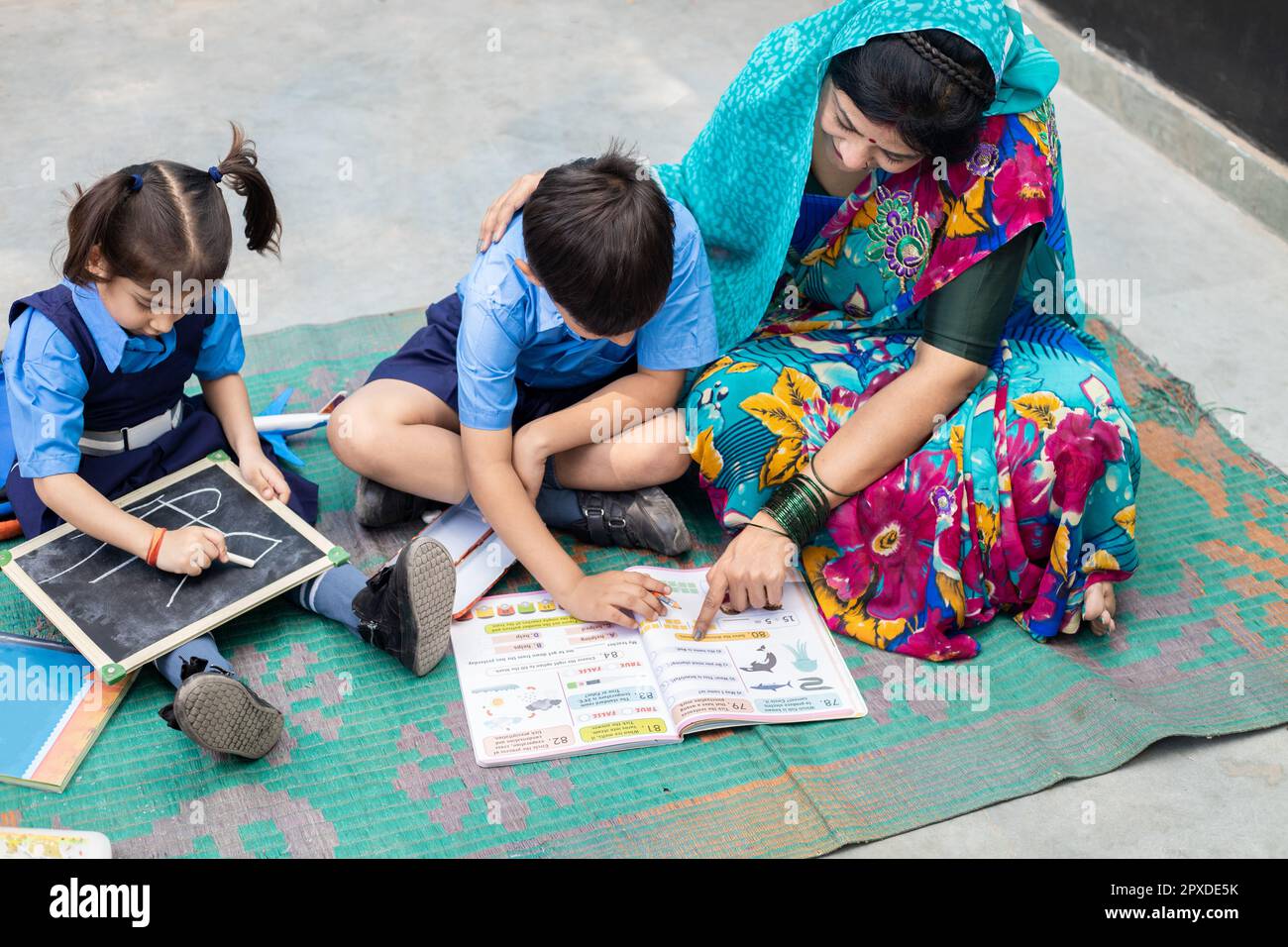 Young indian teacher help little boy and girl students with reading ...