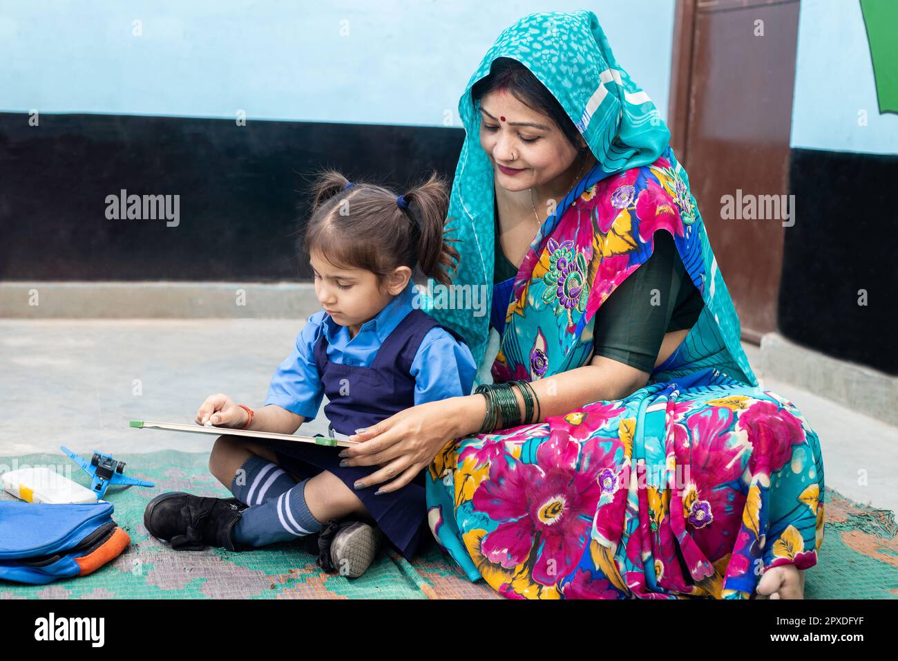 Young indian teacher help little girl student with writing on slate ...