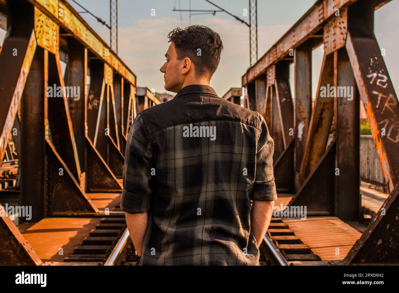 Caucasian teenager standing with his back turned around on train tracks ...