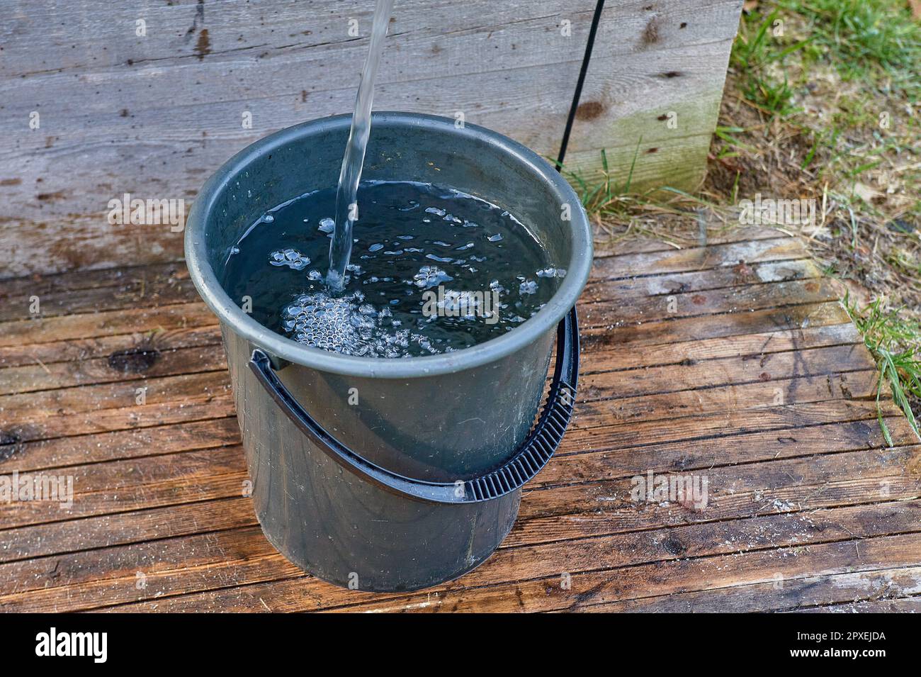a black plastic bucket is filled with water from the pump. High quality ...