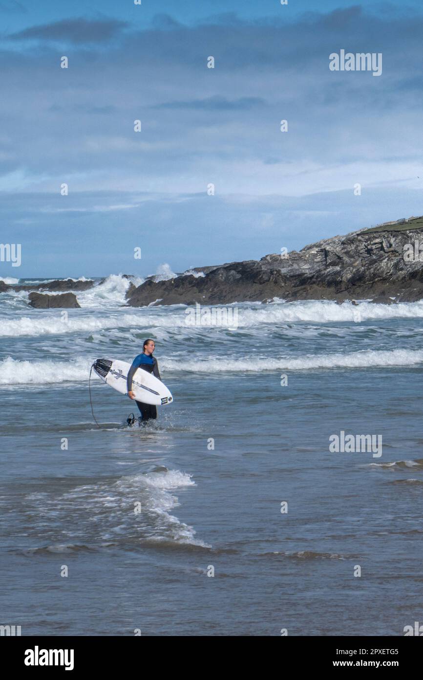 A female surfer carrying her surfboard and walking out of the sea after ...