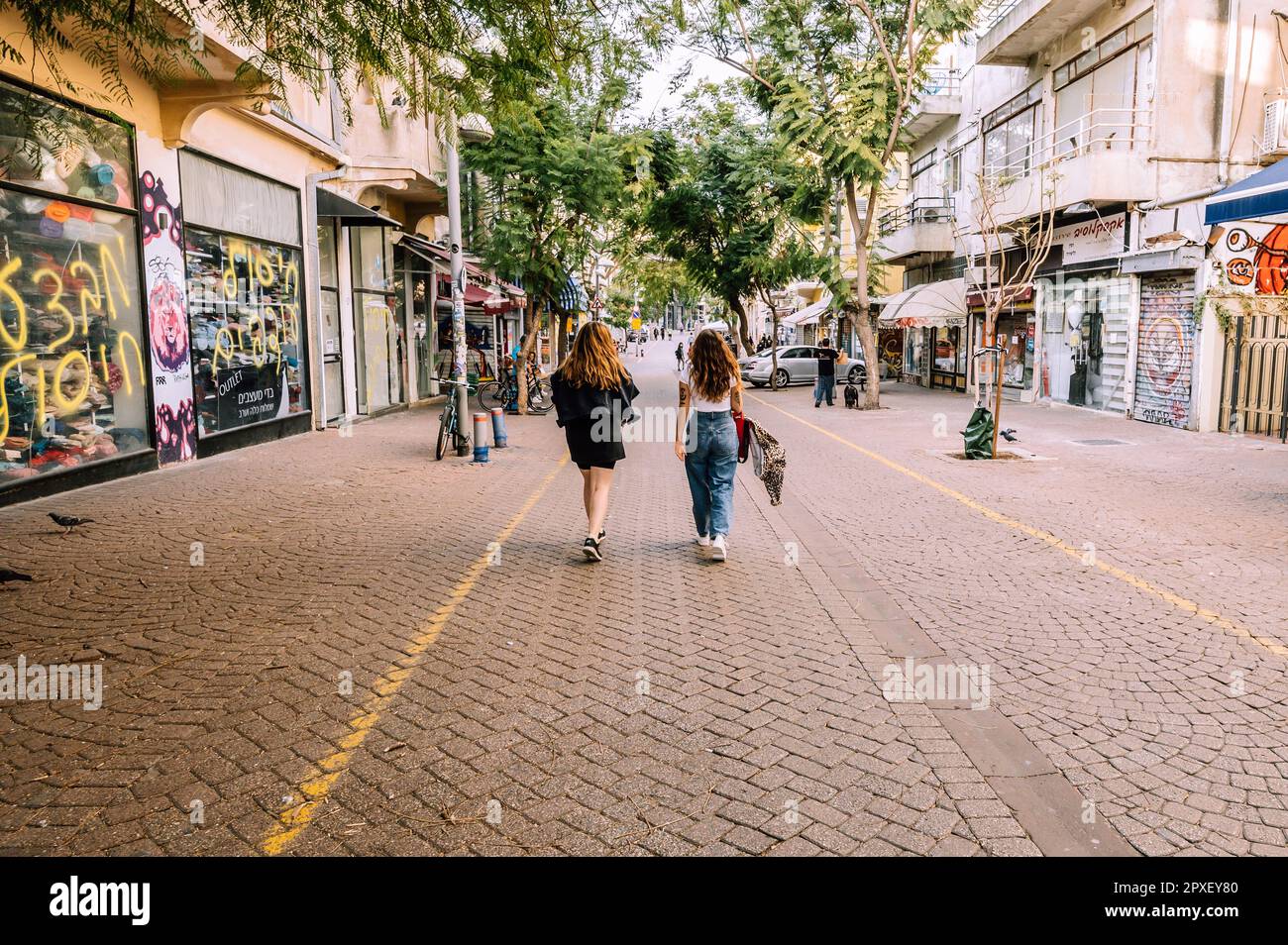 Two female friends walking side by side down a quaint cobblestone ...