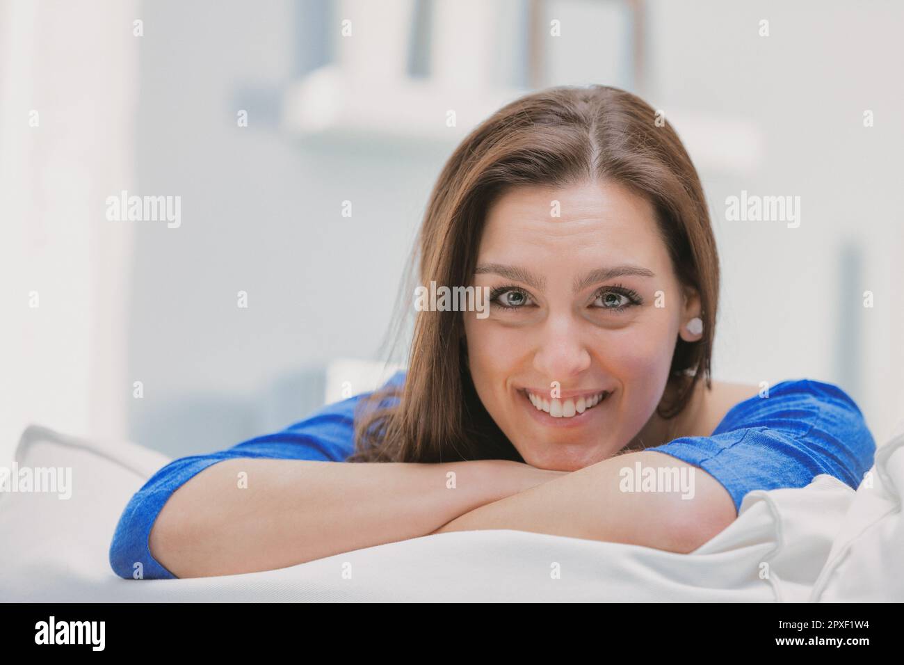 A young, happy, and dreamy woman smiles with her head resting on her crossed arms, which are in ...