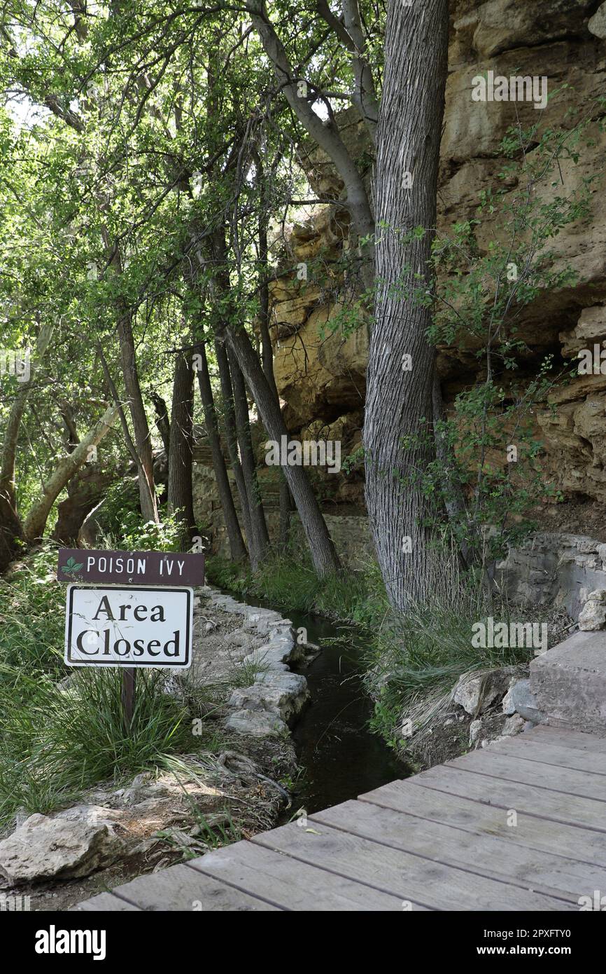 Sign with "Poison ivy" and "Area closed" near a small bridge over water ...