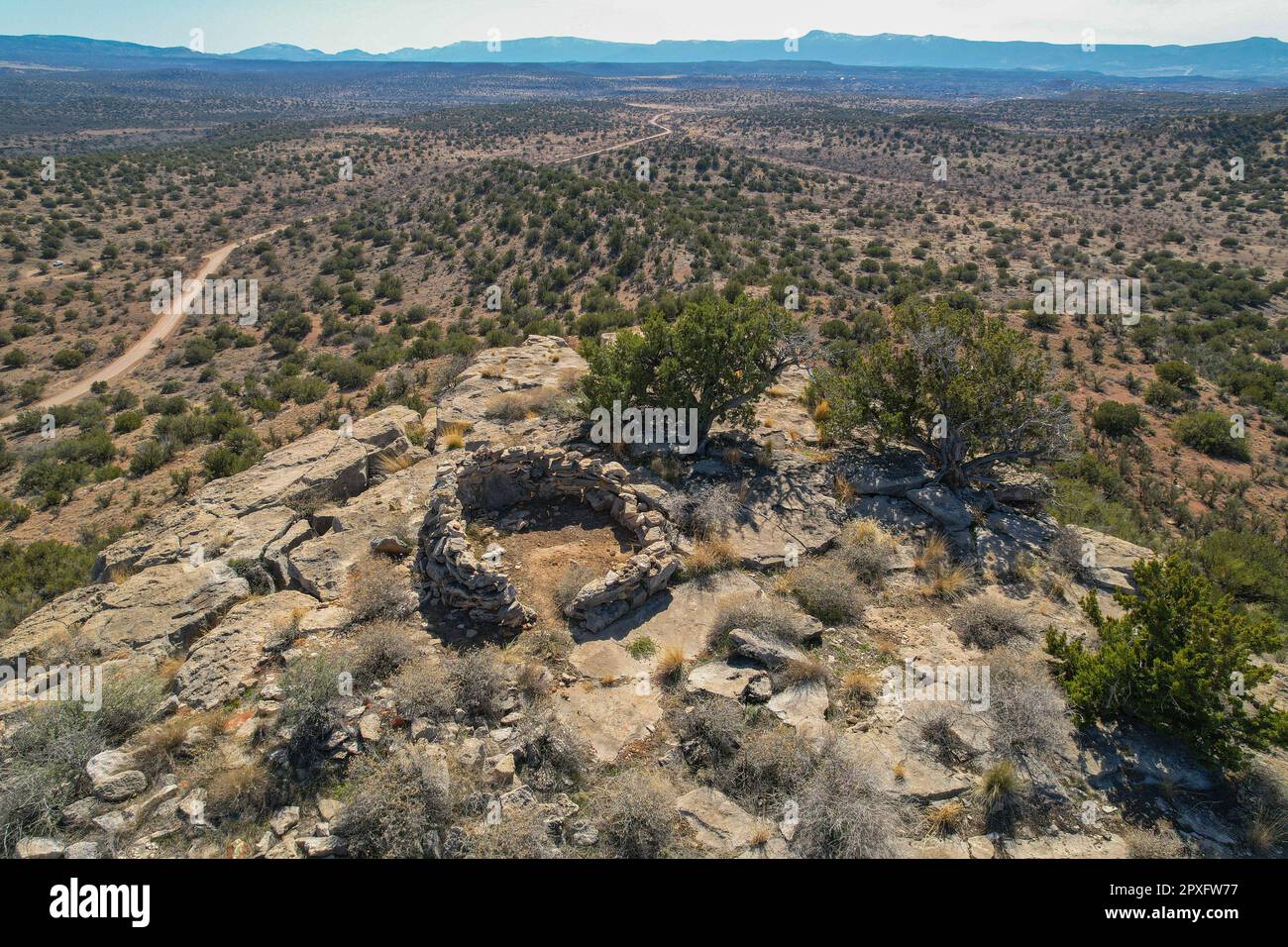 A scene of a Sinagua pueblo situated atop a plateau with trails winding ...