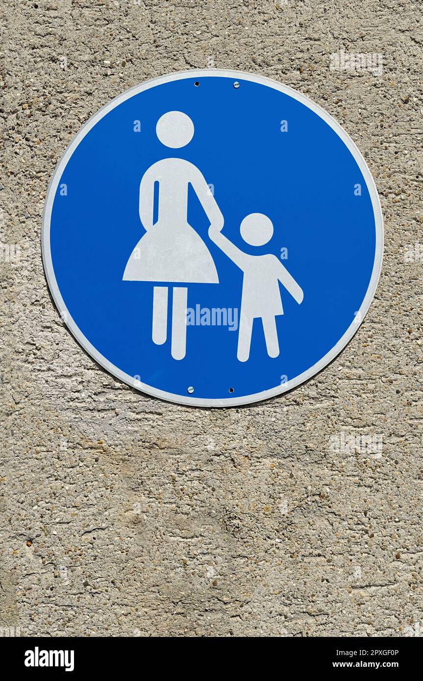 An outdoor stone wall with a blue sign indicating "Parents: Please hold ...