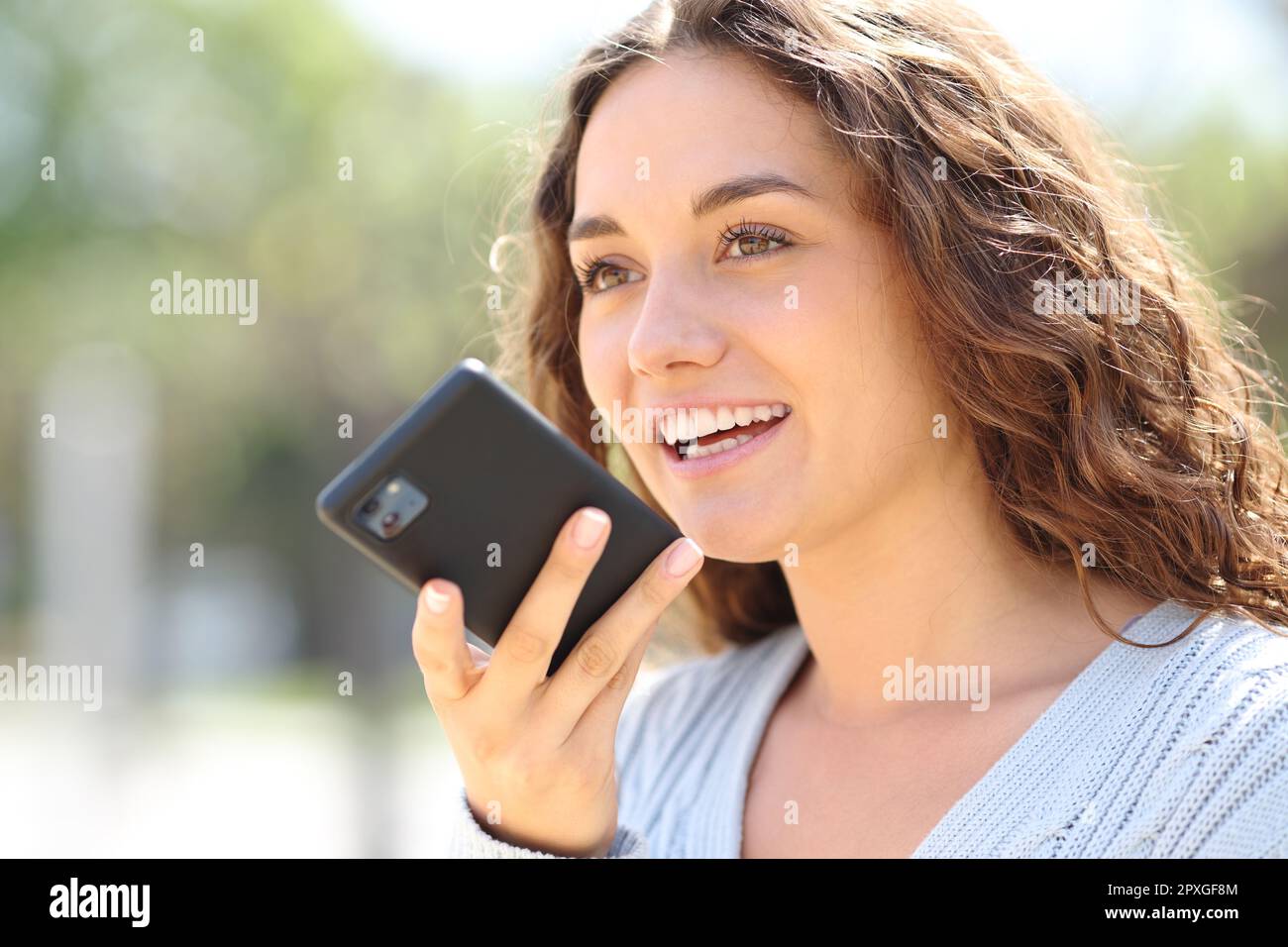 Woman smiling while is dictating message on phone in the street Stock ...