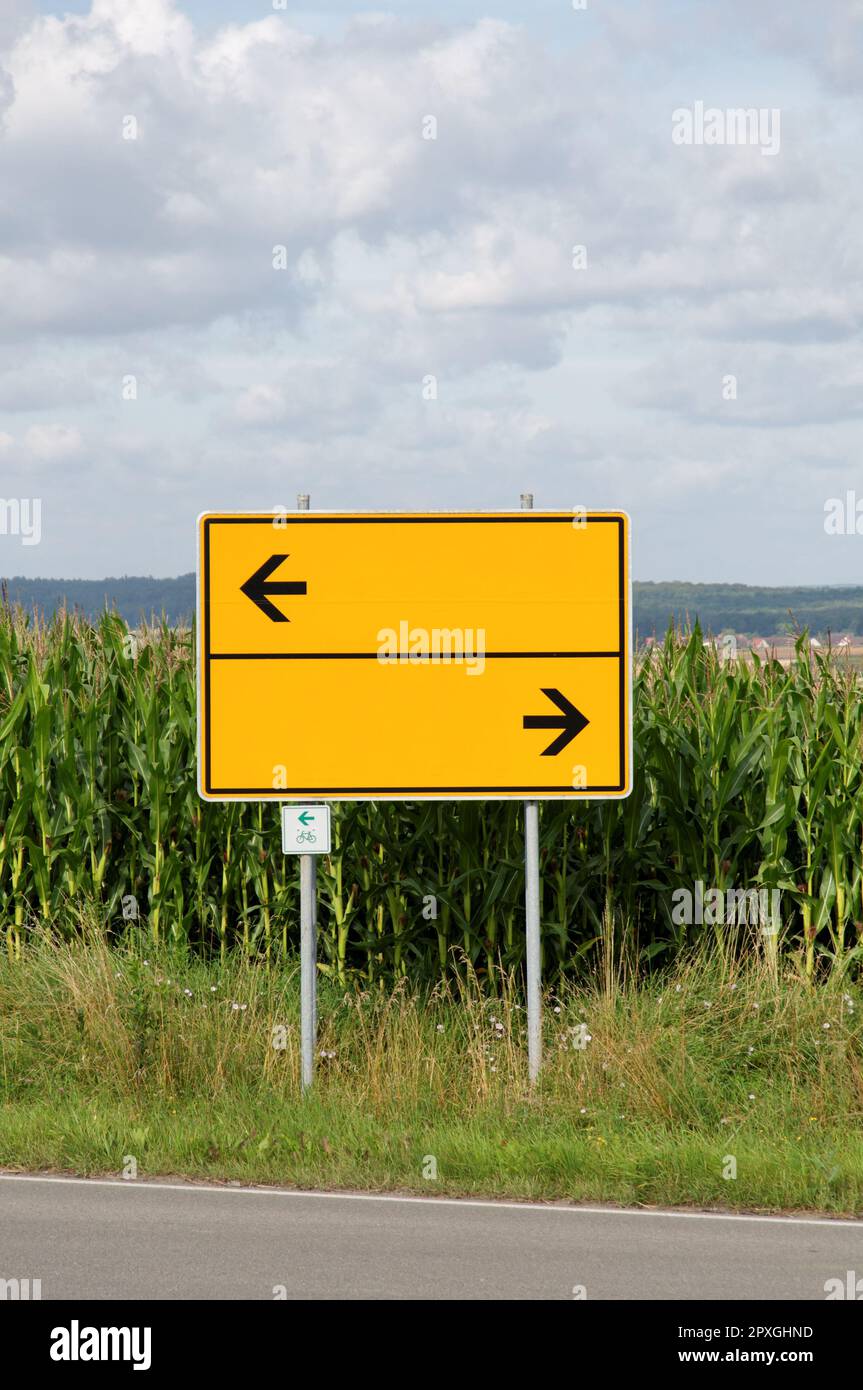 A vertical shot of a yellow direction street sign pointing down a ...