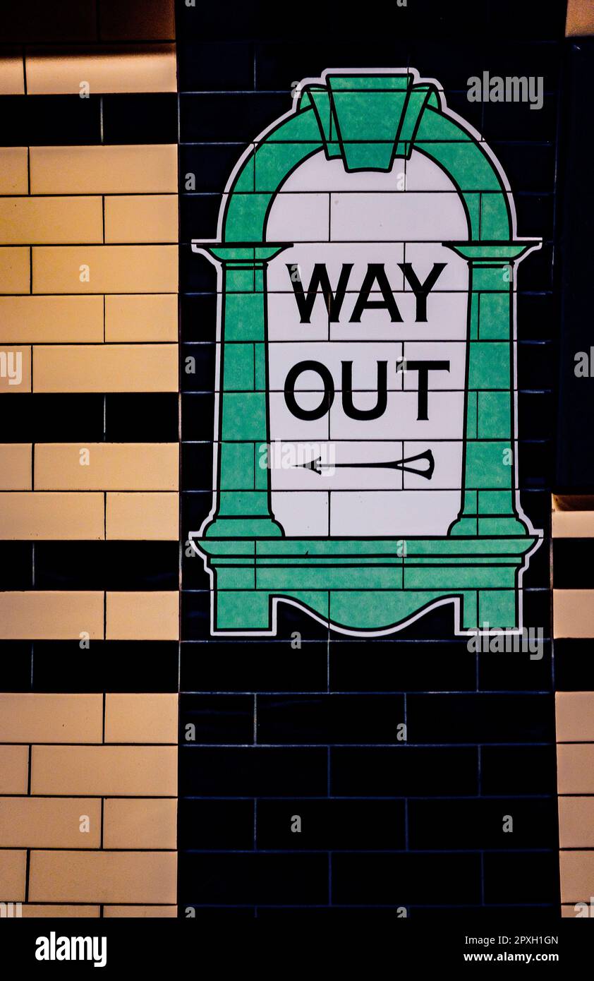 A vertical rectangular way out sign against a brick wall in a subway ...
